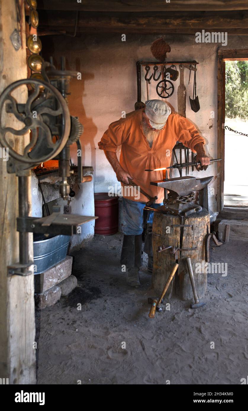 A blacksmith works with an iron and an anvil in the blacksmith shop at ...