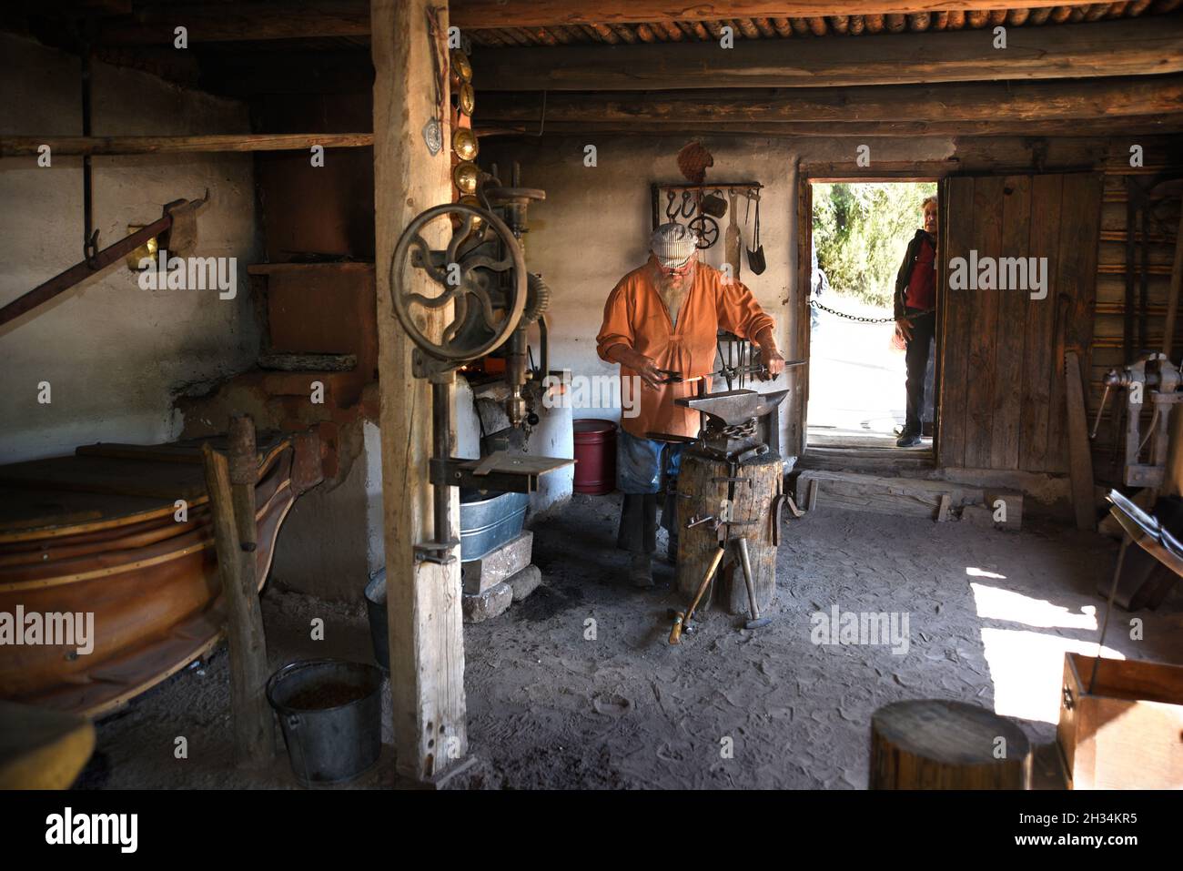 A blacksmith works with an iron and an anvil in the blacksmith shop at ...