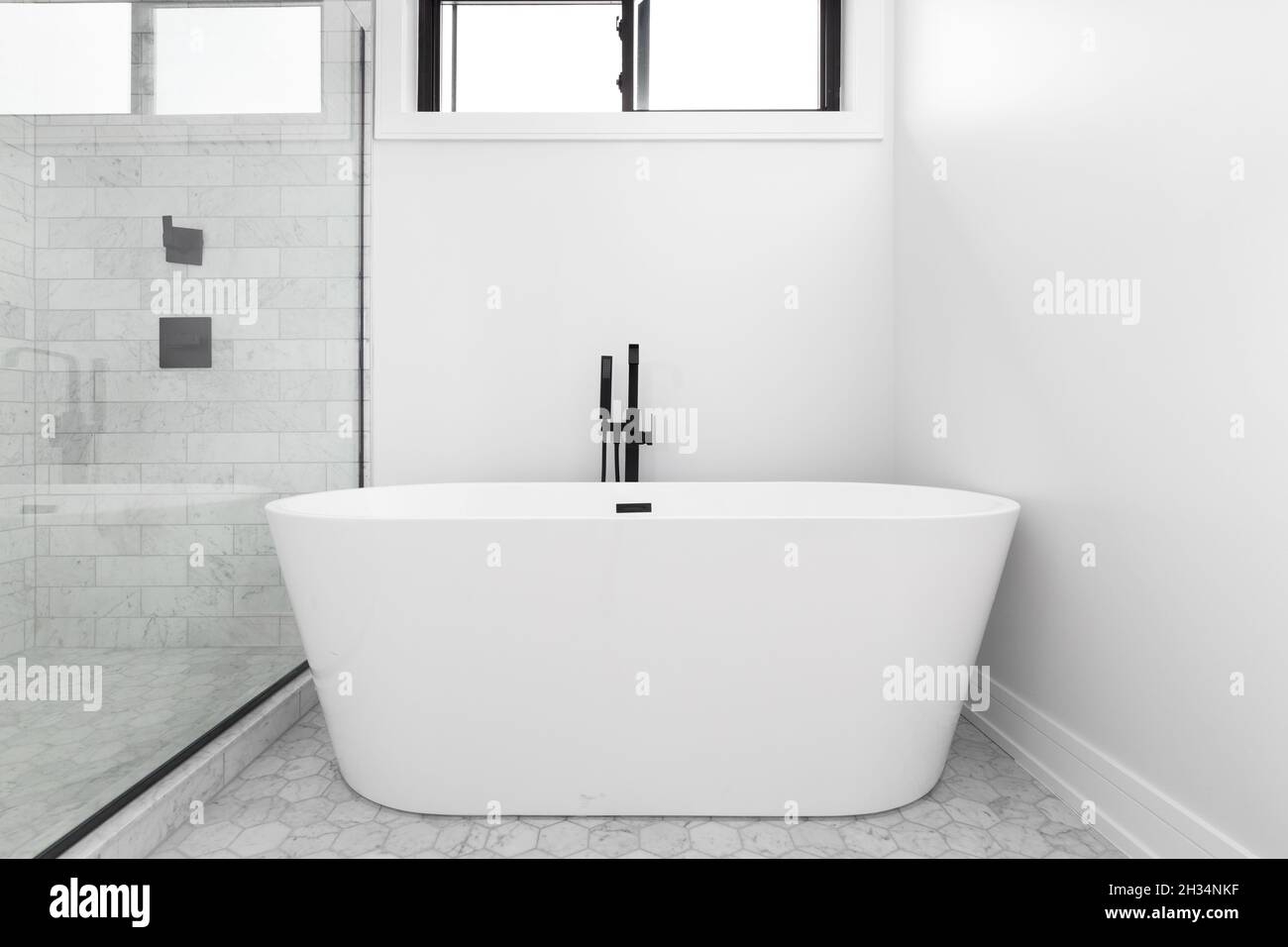 A renovated, standalone tub with a black faucet, small hexagon tiles on ...