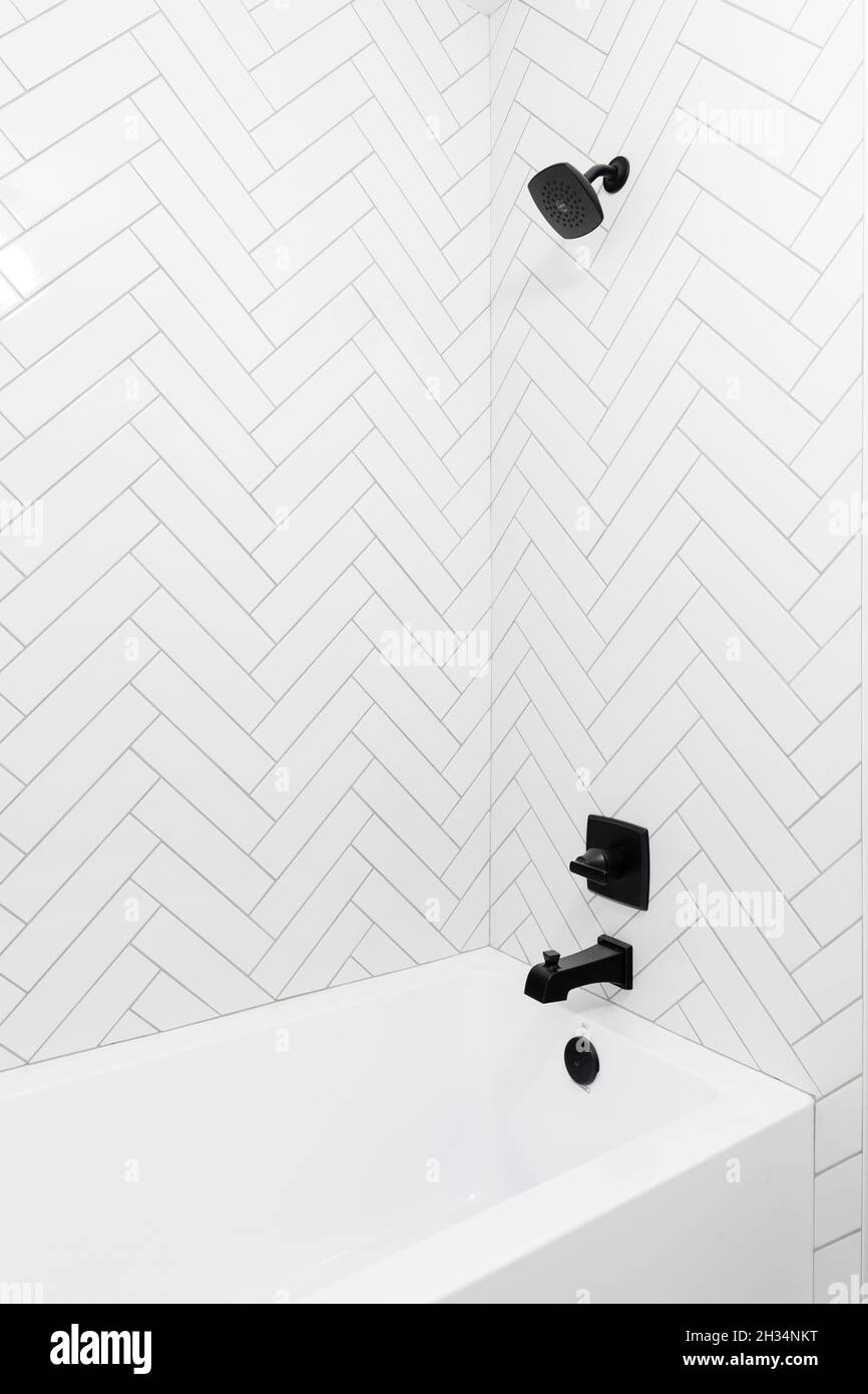 A white herringbone tiled shower with black faucets in a luxury home ...