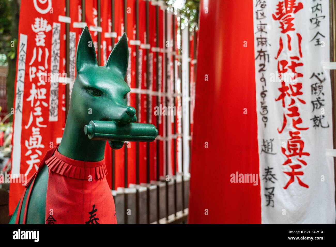 A statue of Inari Kitsune or fox goddess, wearing a red bib and ...