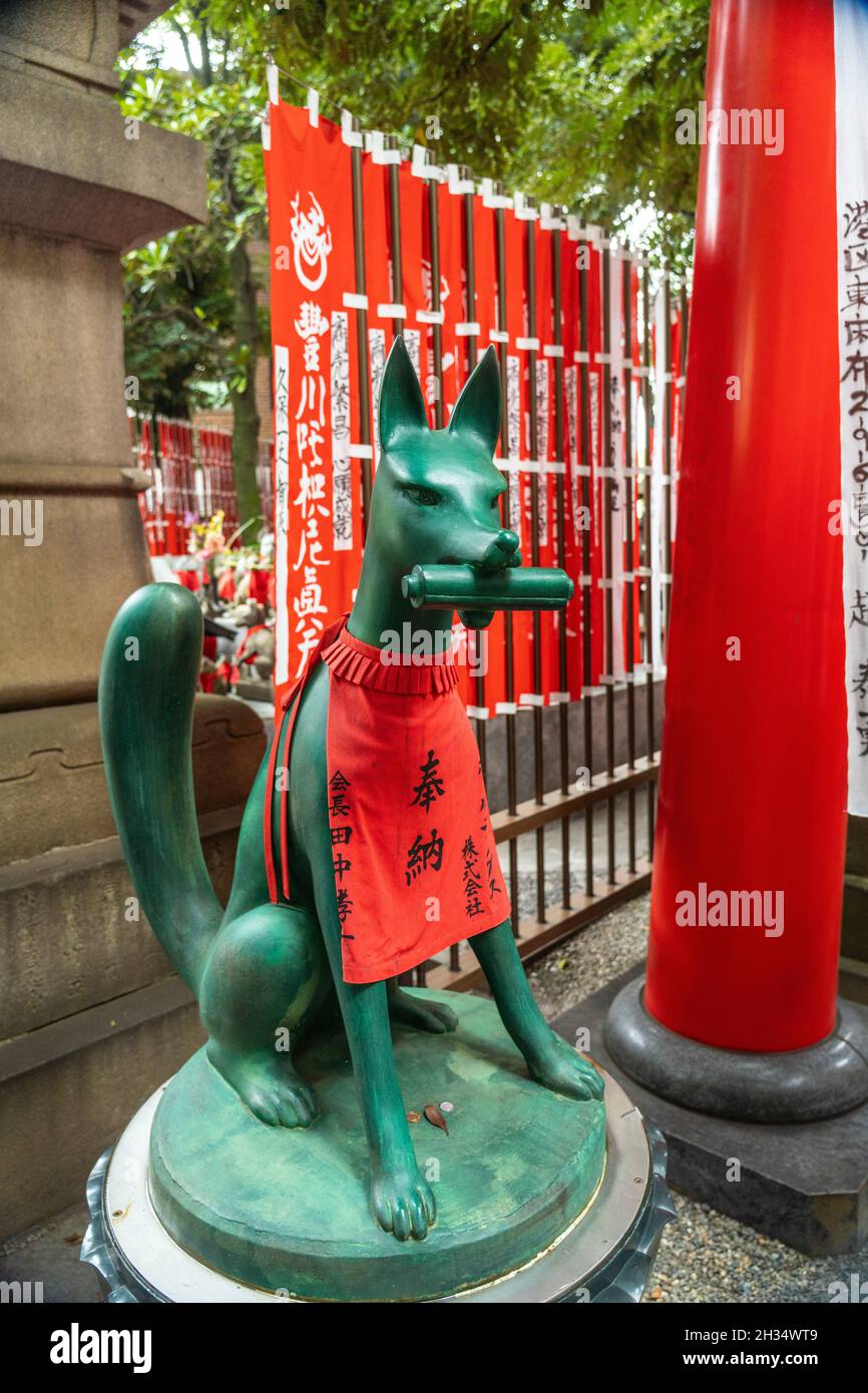 A statue of Inari Kitsune or fox goddess, wearing a red bib and ...