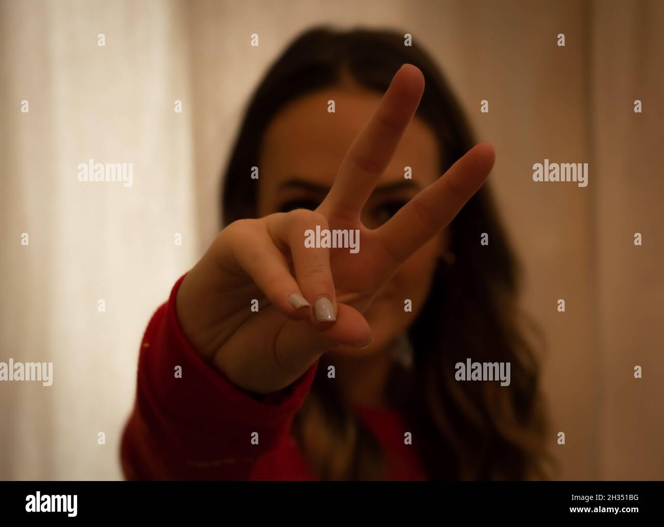 Portrait of a young brunette girl showing the peace sign at home Stock ...