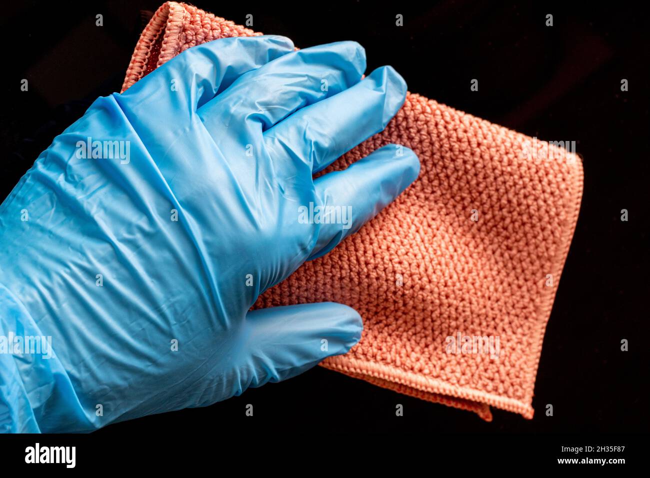 A hand in a blue protective glove wiping dust, dirt from a black ...