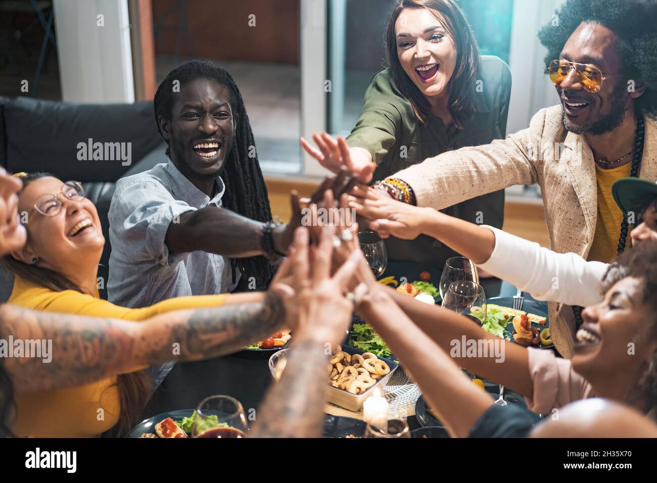 A multiracial group of adults has fun sitting at the table for dinner ...