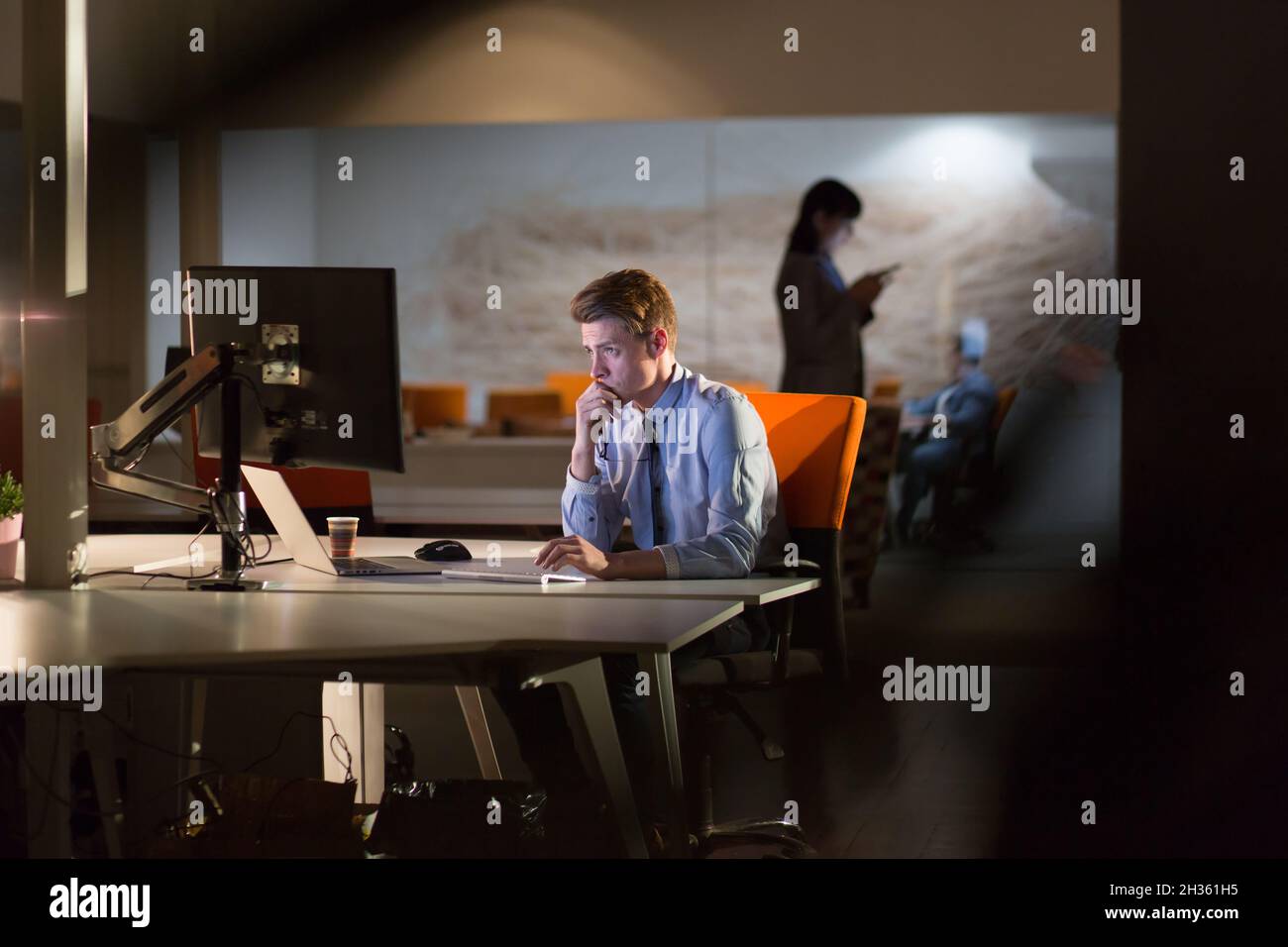 Young man working on computer at night in dark office. The designer ...