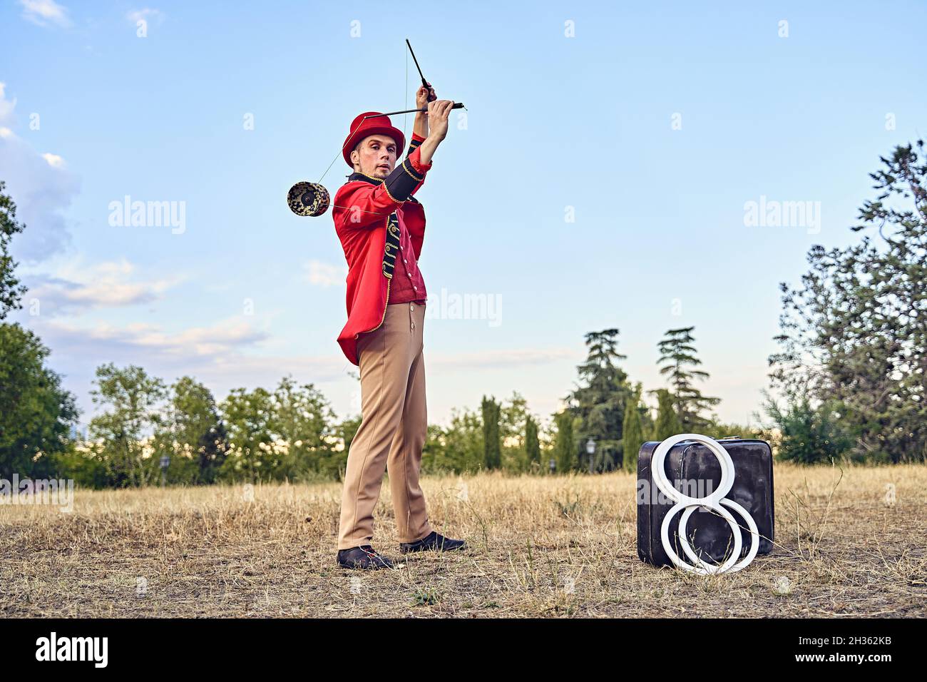 Full body funny male juggler in red costume showing trick with diabolo ...