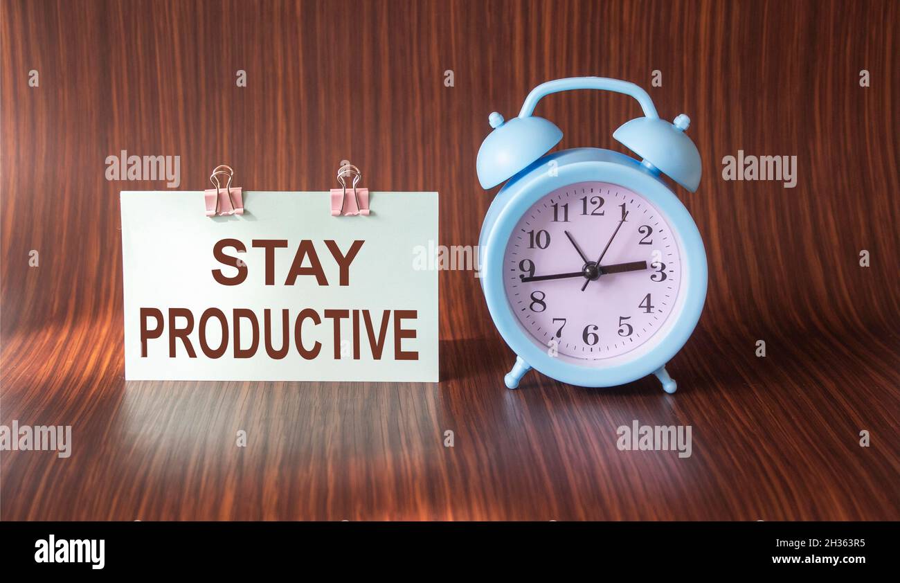 Stay productive, text on sticker and wooden background with blue alarm ...