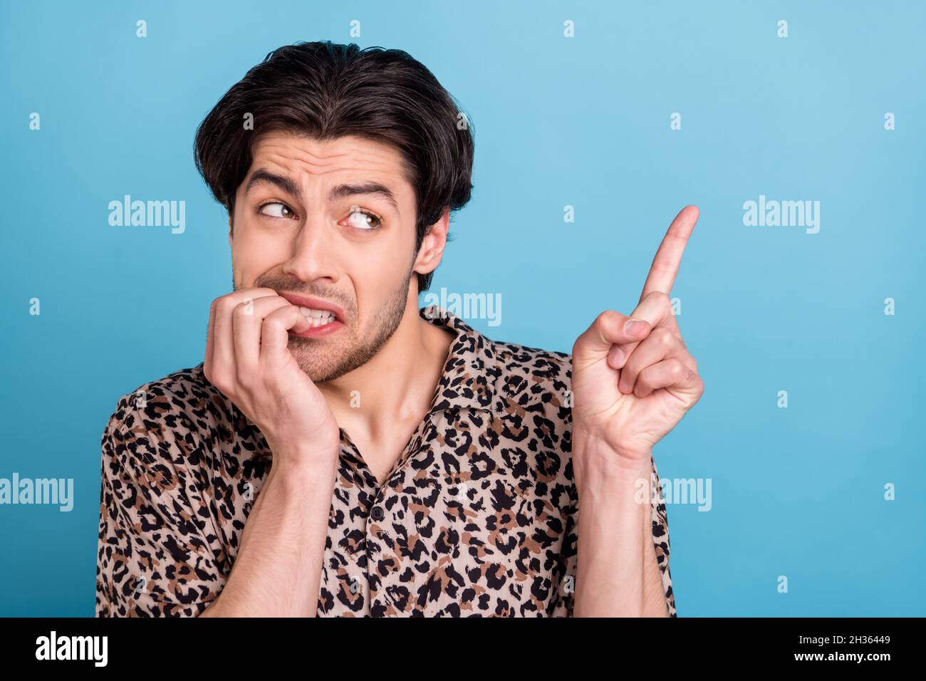 Portrait of attractive desperate scared guy pointing up biting nails ...