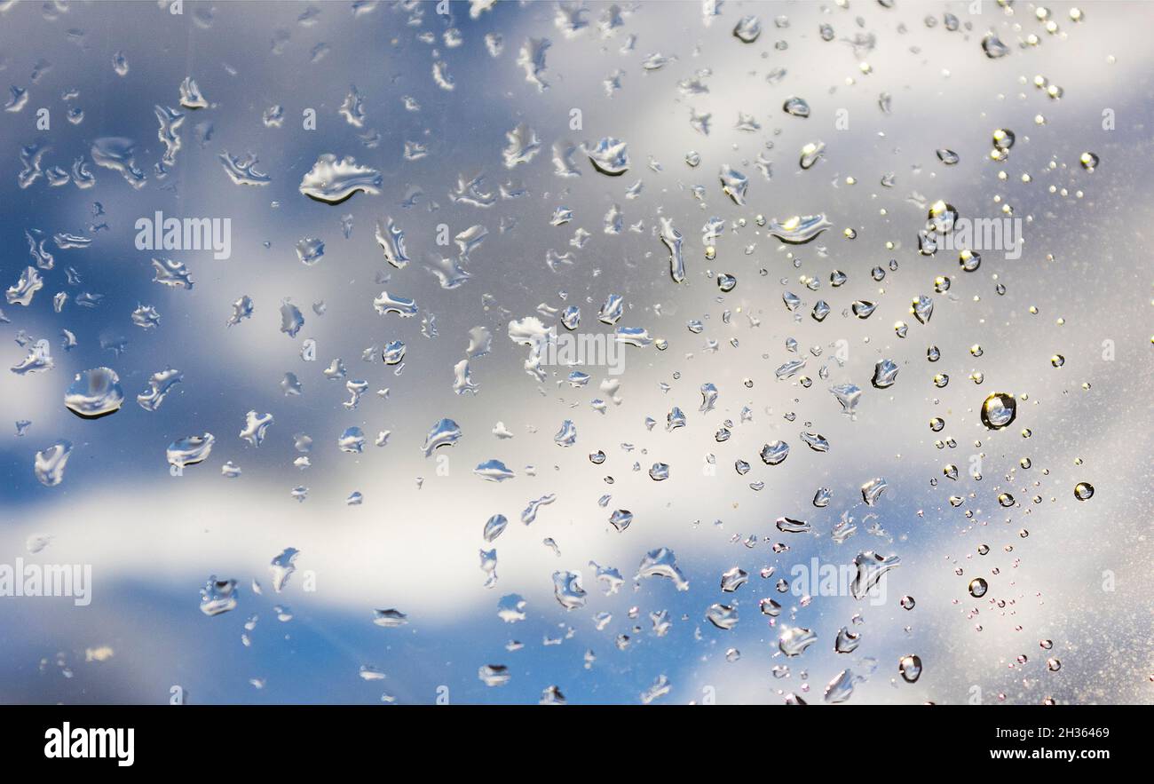 Raindrops on the window pane, blue sky and clouds visible through the transparent glass of the ...
