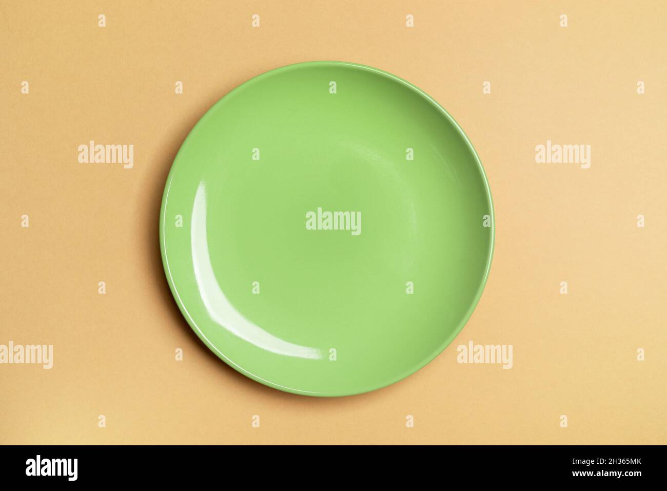 One green empty plate in center of beige background. View from above ...