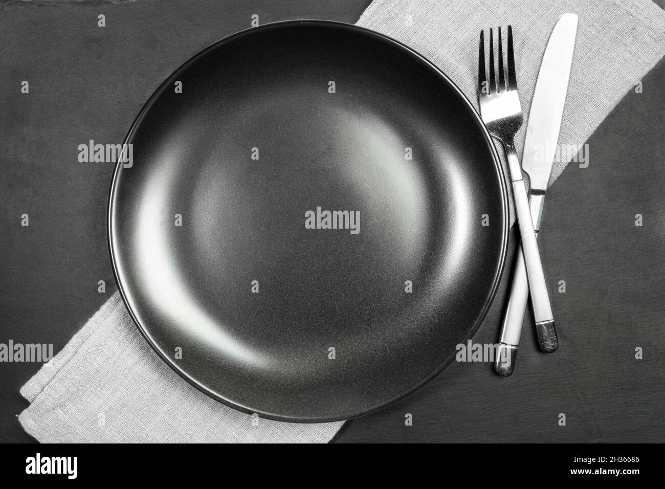Empty blank black plate and cutlery on grey diagonal cooking towel on ...