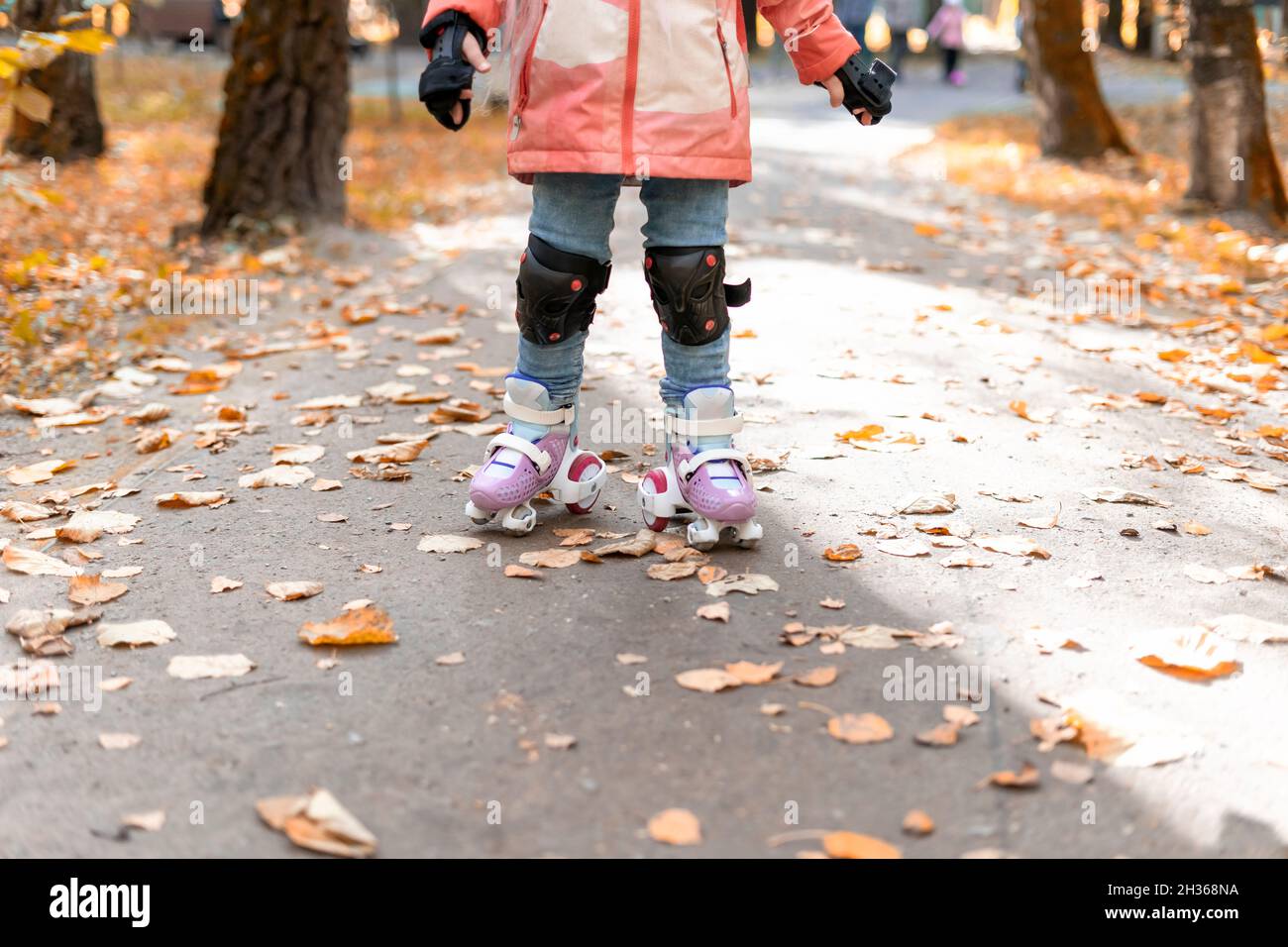 little girl in protective clothing in an autumn park is rollerblading ...