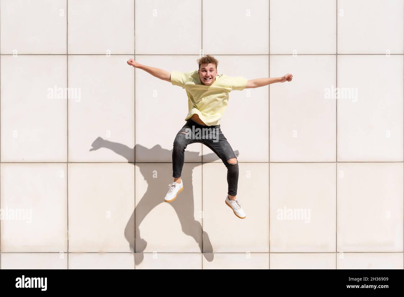 Young man in a yellow T-shirt with curly hair jumping and casting his ...