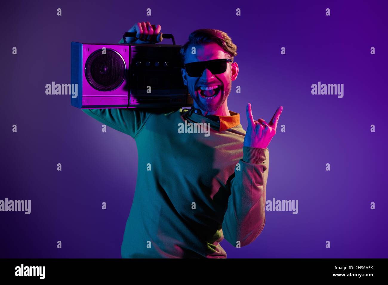 Photo of funky happy young cheerful man make rock sign hold boombox ...
