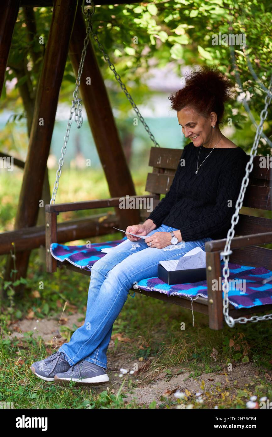 Woman reading an amusing letter while sitting in a swing Stock Photo ...