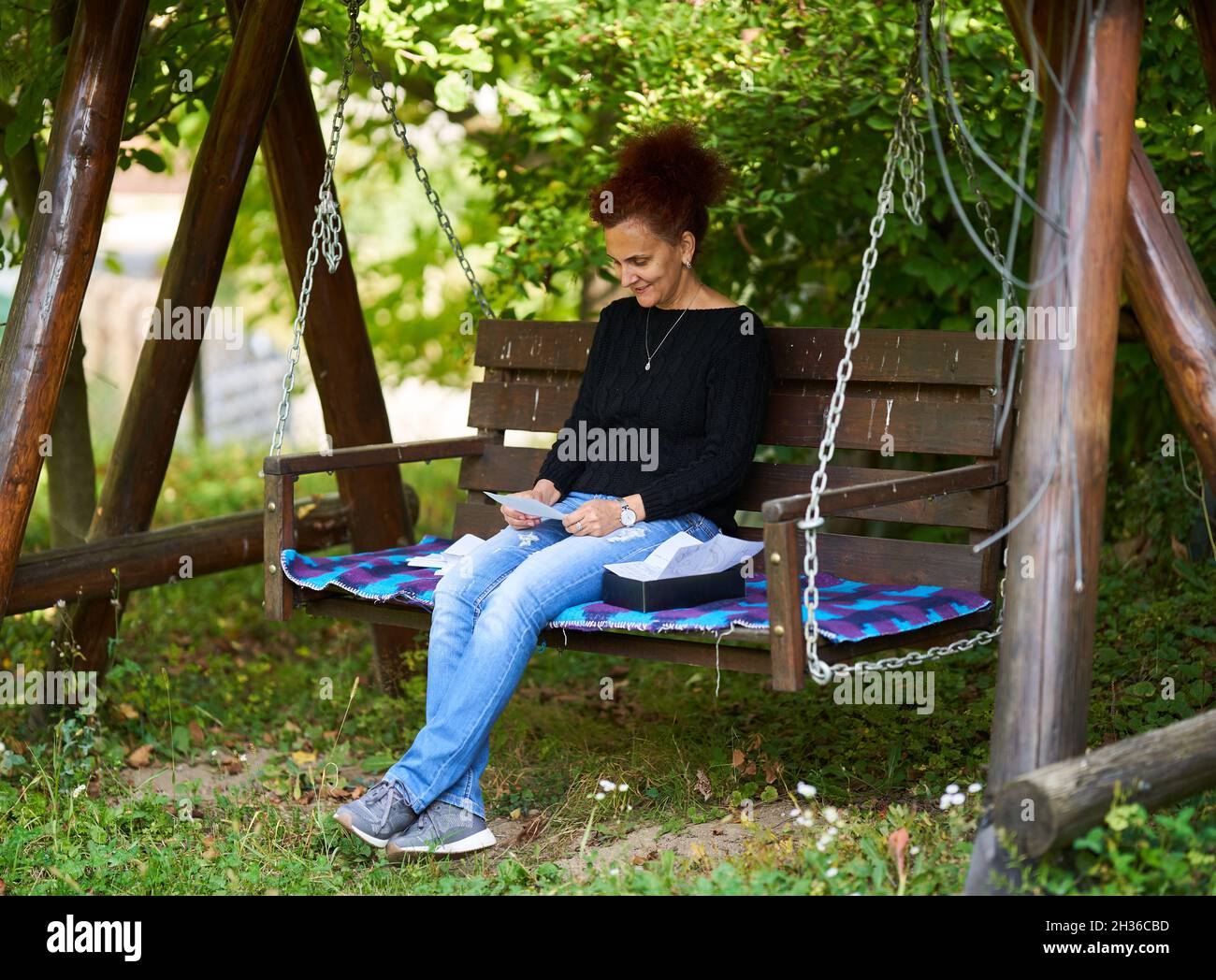 Woman reading an amusing letter while sitting in a swing Stock Photo ...