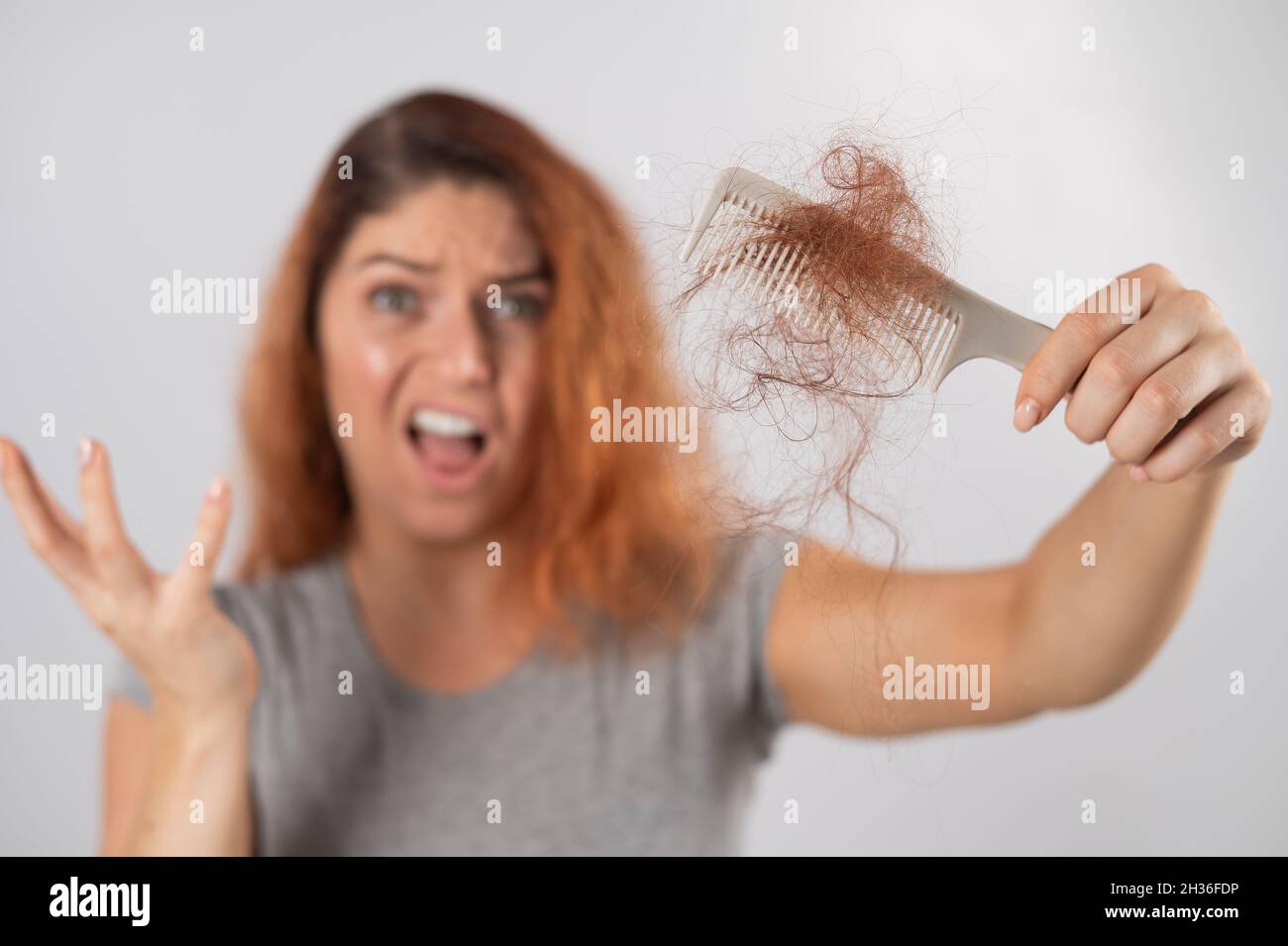 Caucasian woman with a grimace of horror holds a comb with a bun of ...