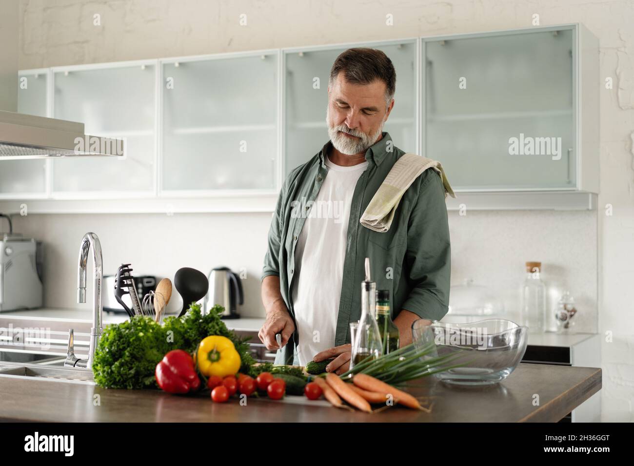 Handsome senior man cooking at home preparing salad in kitchen Stock ...