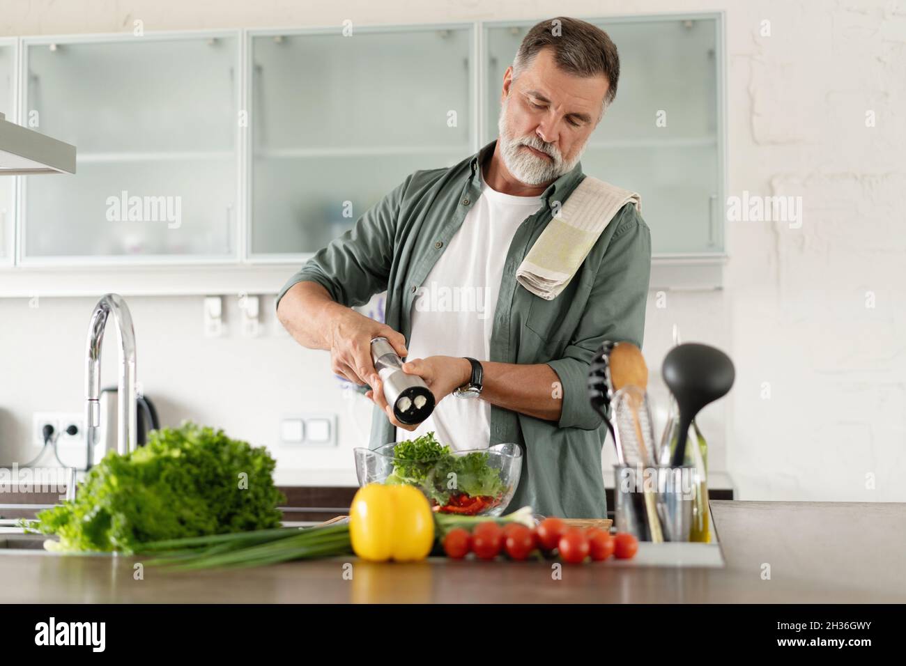Mature man pouring salt over healthy salad in kitchen for delicious ...