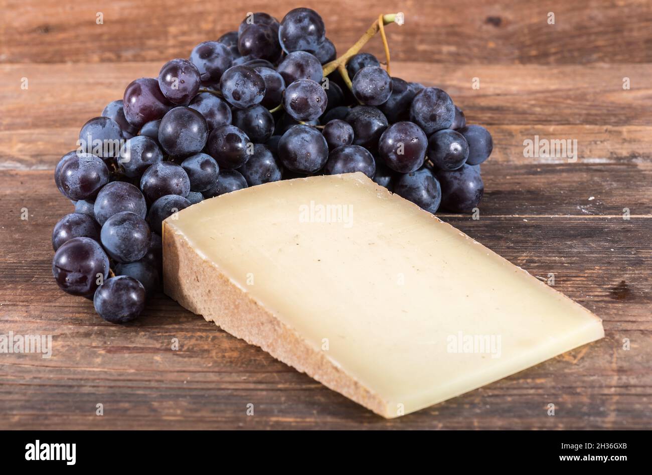 French comté cheese with black grapes on wooden background Stock Photo ...