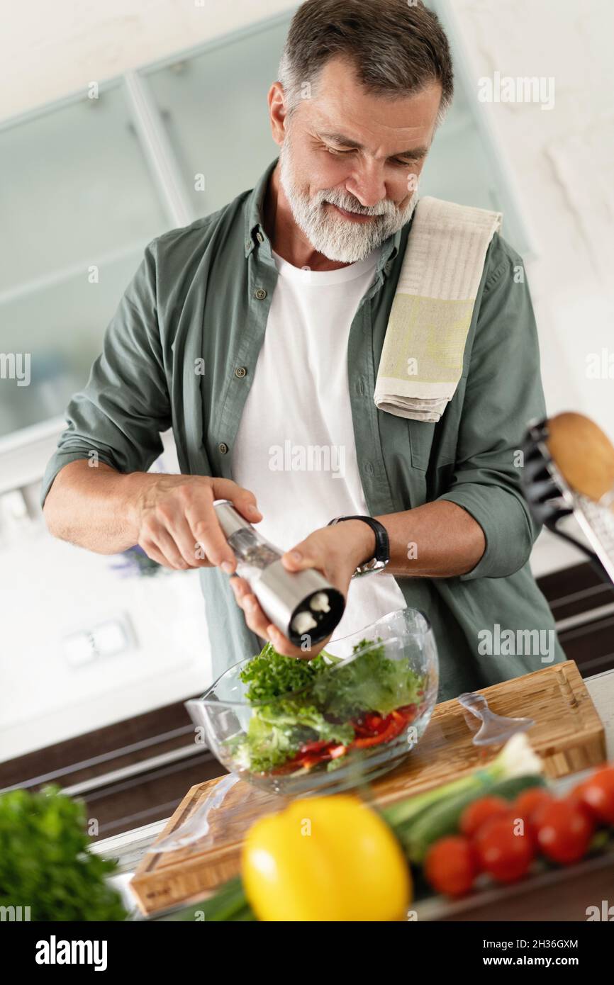Mature man pouring salt over healthy salad in kitchen for delicious ...