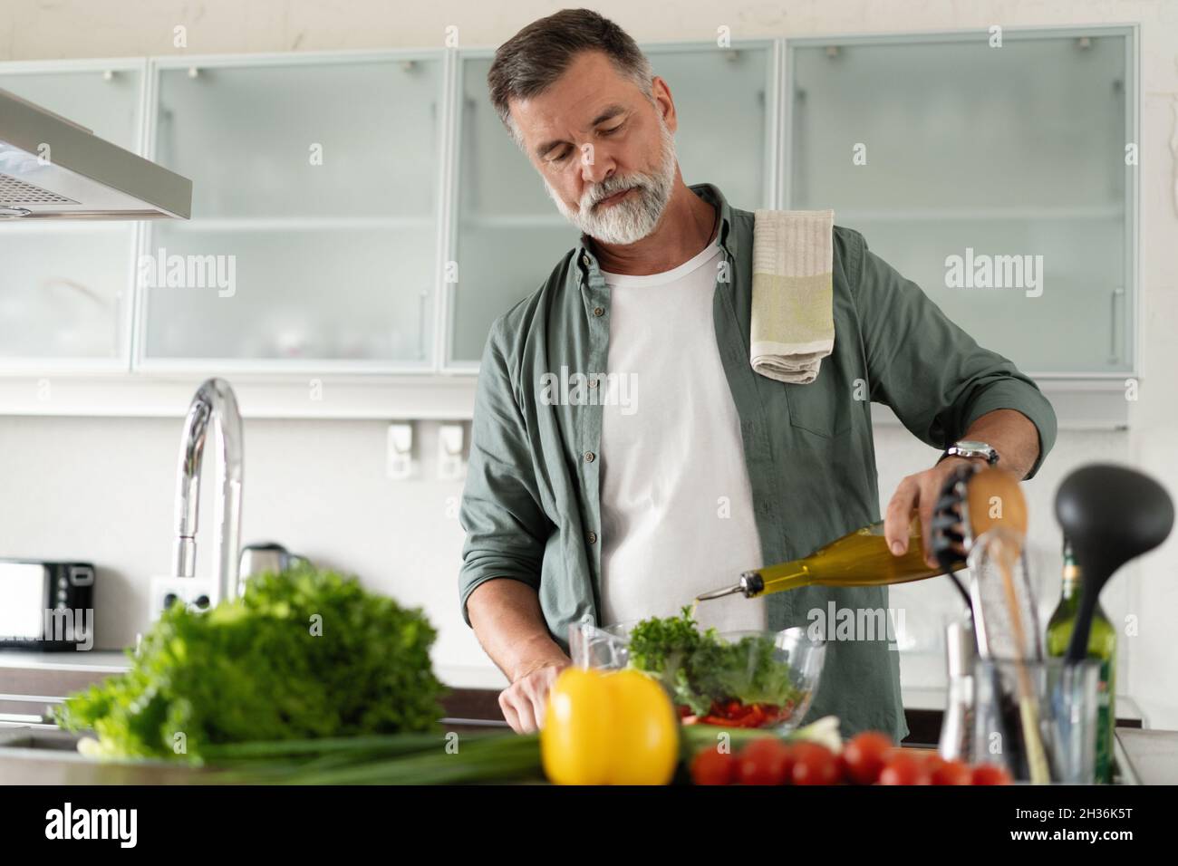 Mature man cooking vegetables salad in home kitchen. Male hands pouring ...