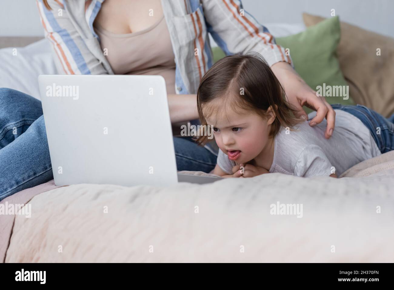 Blurred woman touching kid with down syndrome near laptop on bed Stock ...