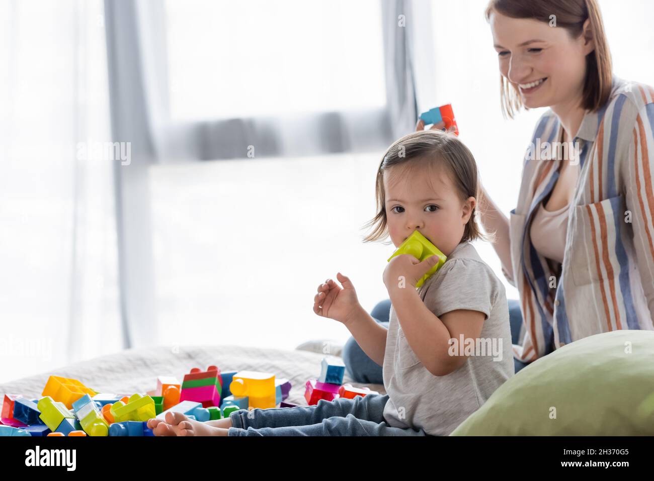 Kid with down syndrome playing building blocks near smiling mother on ...