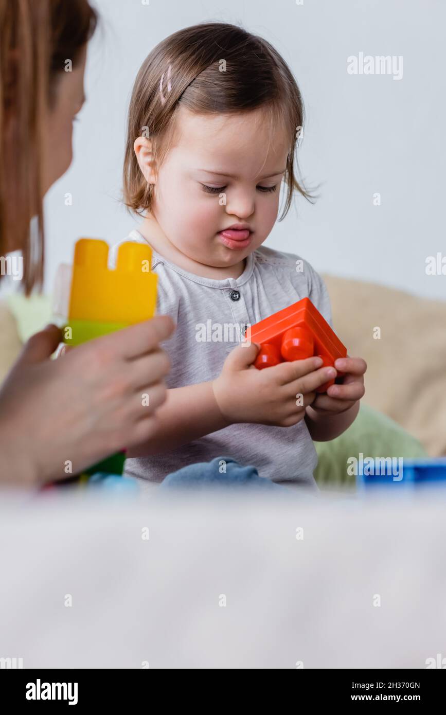 Toddler girl with down syndrome holding building block near mother at ...