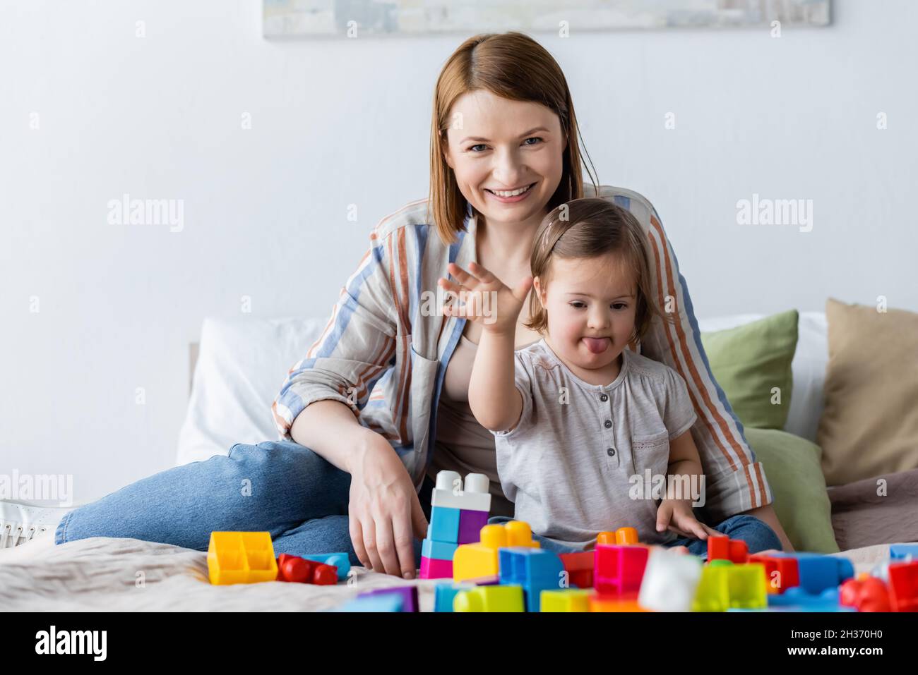 Woman and child with down syndrome waving hand at camera near building ...