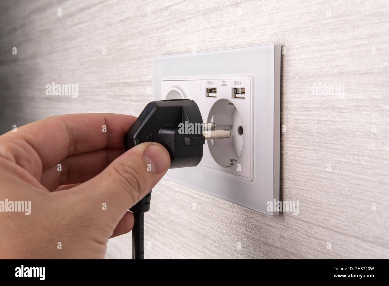 Hand plugging in an electric cord into a white plasticmodern socket or ...