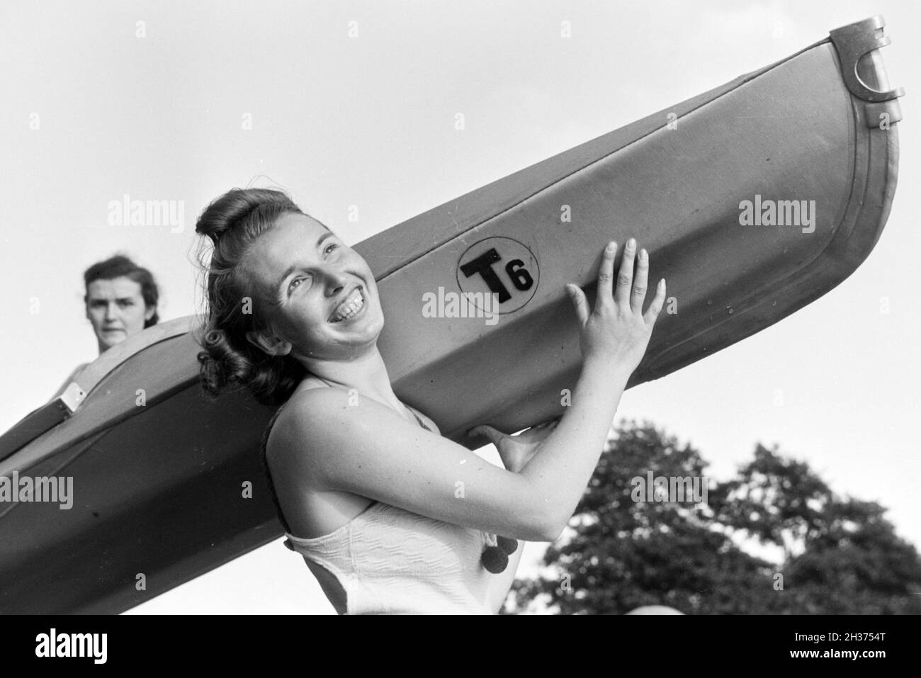 Junge Frau trägt im Badeanzug lachend ein Boot / Klepper T6 ...