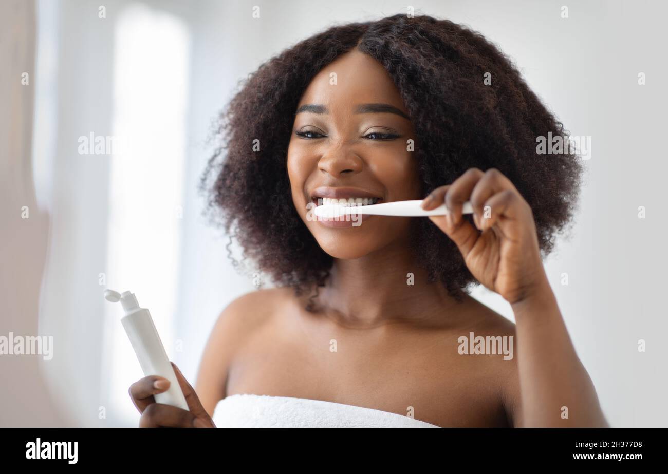 Pretty young black woman brushing teeth with toothpaste at home ...