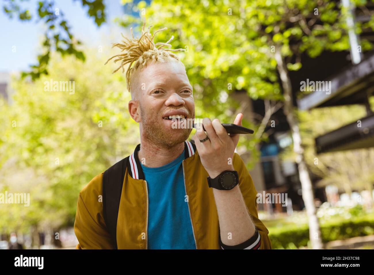 Happy albino african american man with dreadlocks in park talking on ...