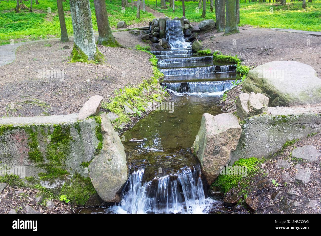 A cascade of a stream flows onto stone steps in a city park. Europe ...