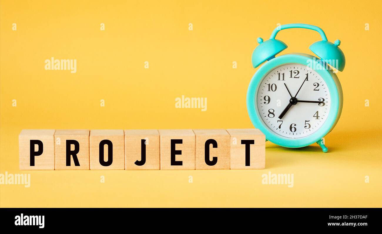 Project word written in wooden cube and yellow background with clock ...