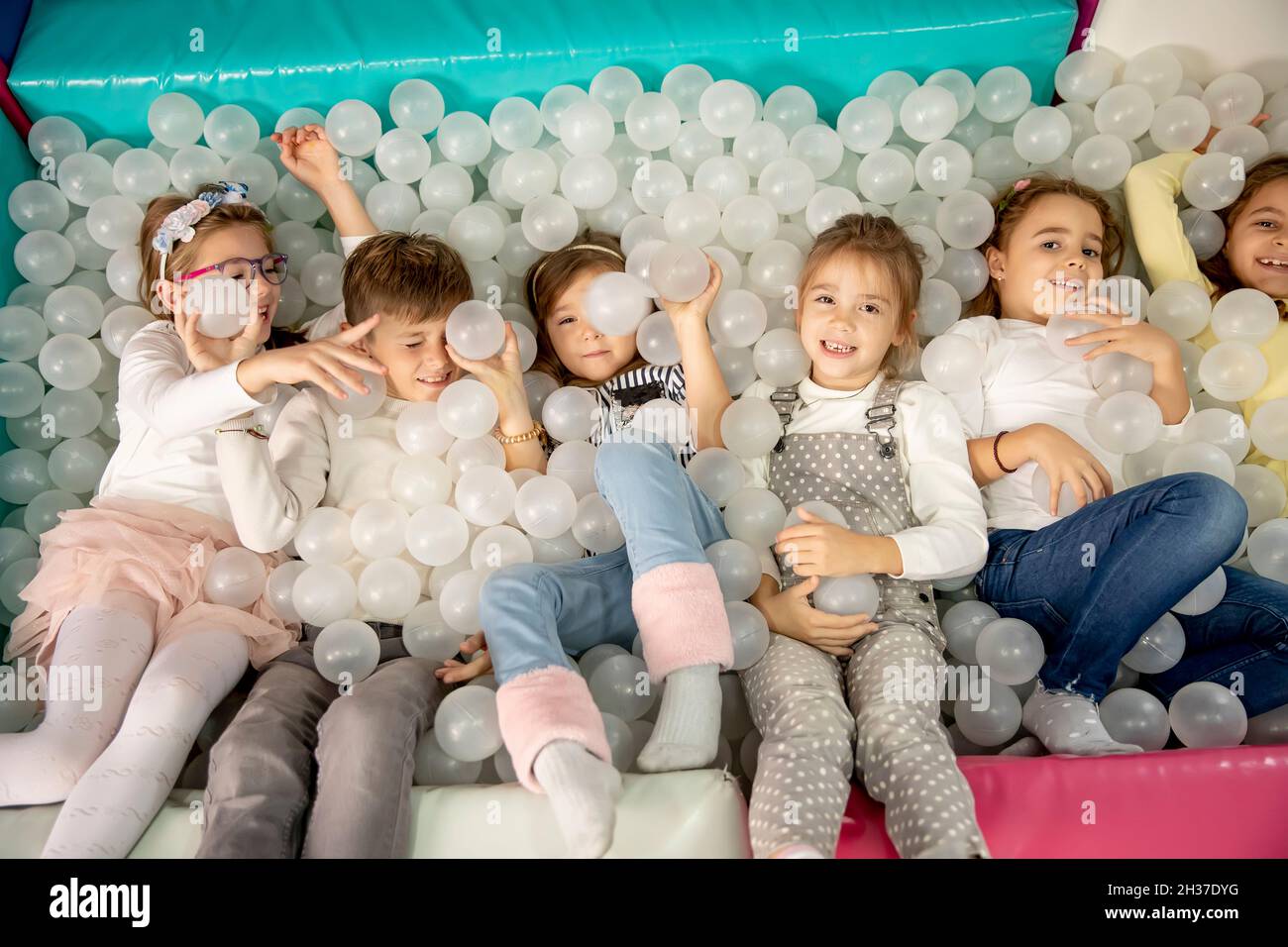 Group of happy little kids in ball pit smiling happily at camera while ...