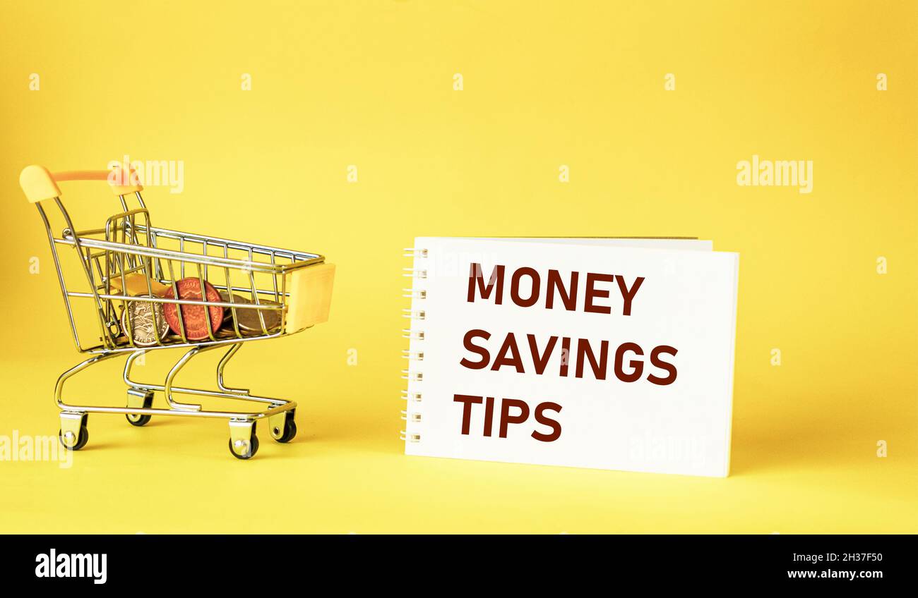 MONEY SAVING TIPS text on notepad, next to a small cart with coins on a ...