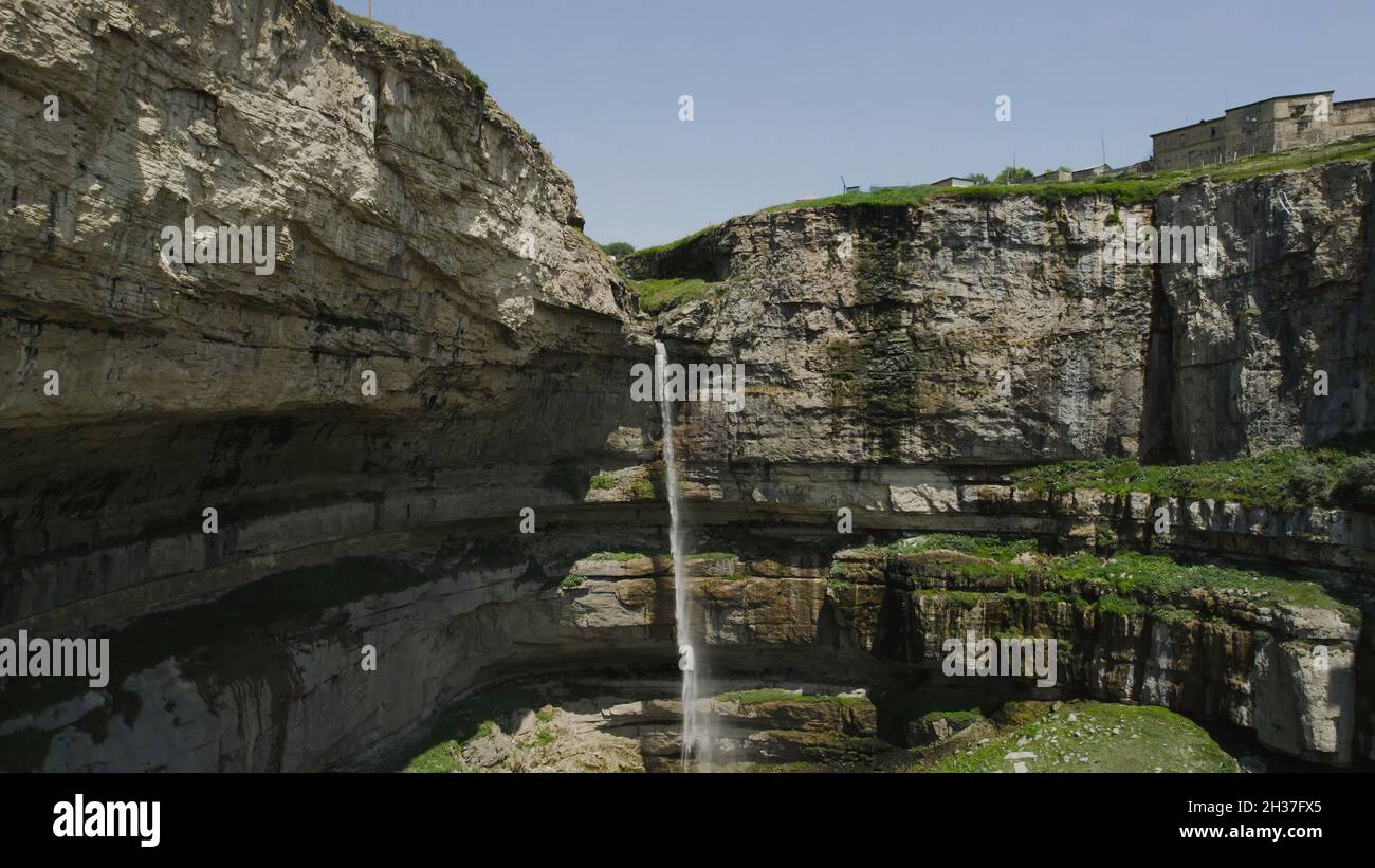 Narrow waterfall falls from high cliff. Action. Top view of water from ...