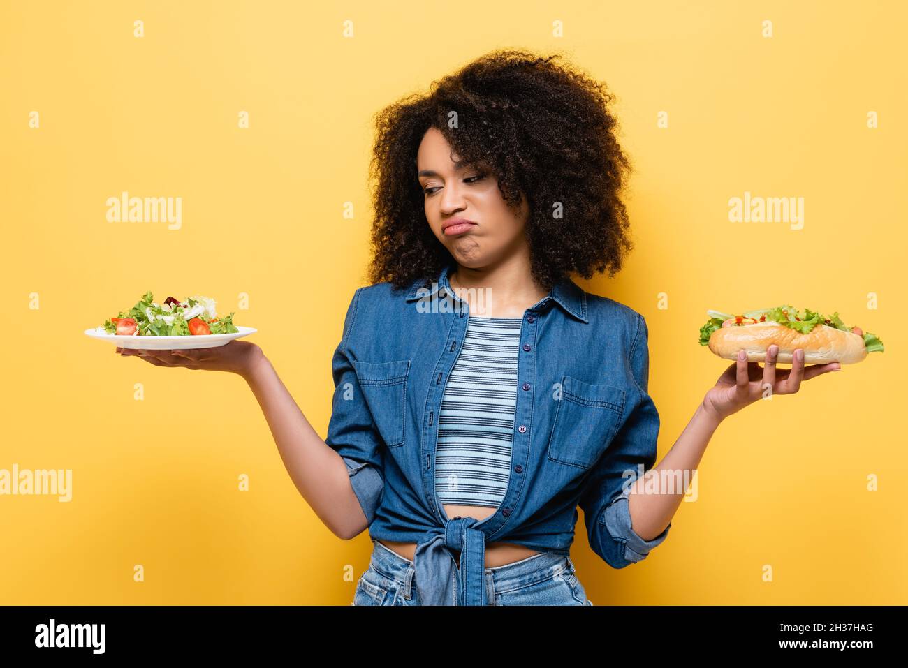 displeased african american woman looking at vegetable salad while ...