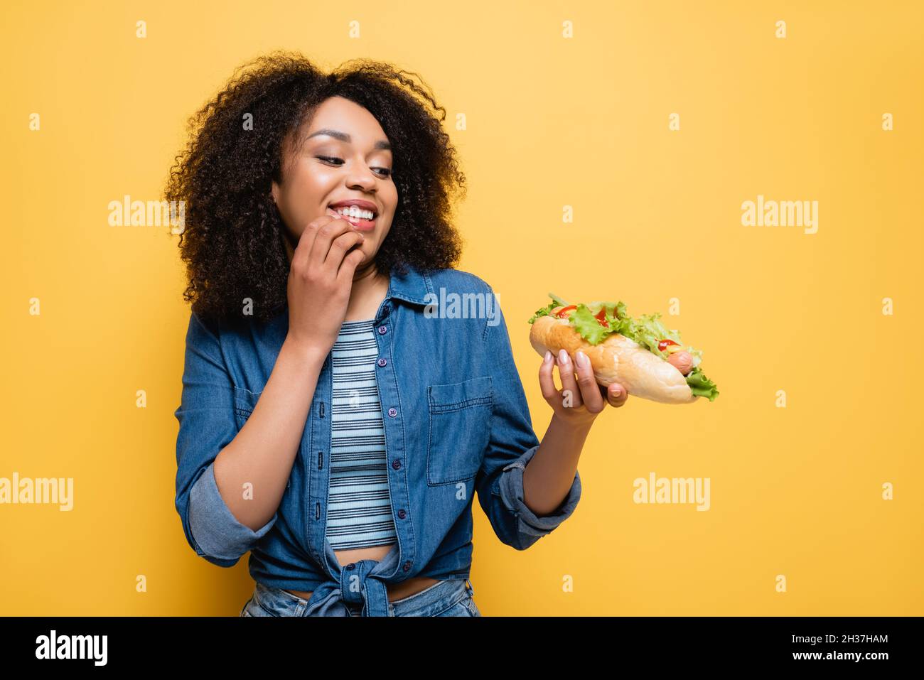 joyful african american woman looking at delicious hot dog isolated on ...
