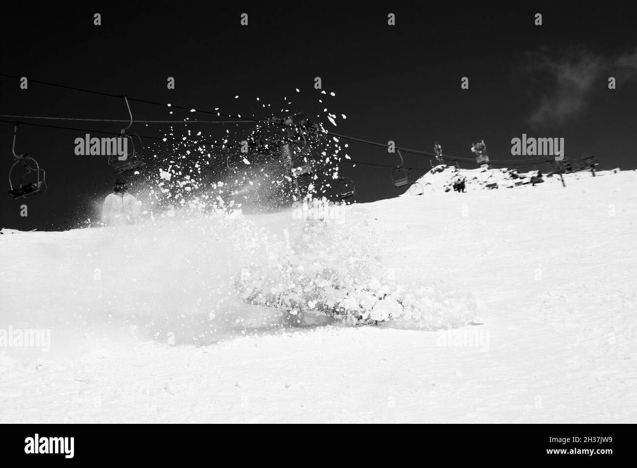 Snowboarder fall down with snow splashes on snowy ski slope and chair ...