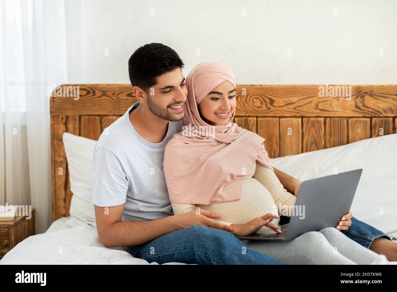 Cheerful pregnant arab couple using laptop computer, watching movie ...
