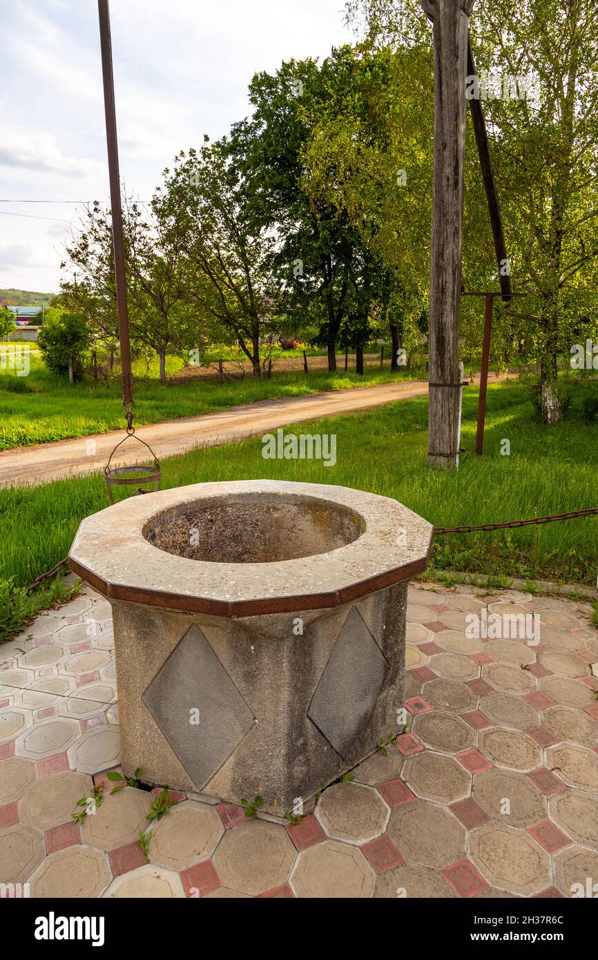Concrete well casing, water intake point by the roadside. Garden in the ...