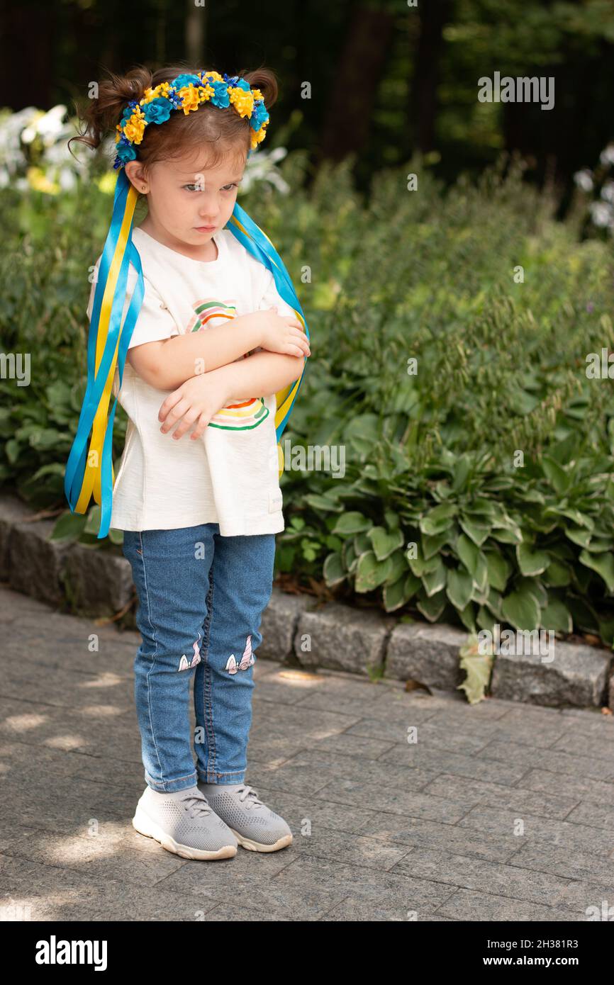 A little sad girl with Ukrainian folk ornaments on her head hugs ...