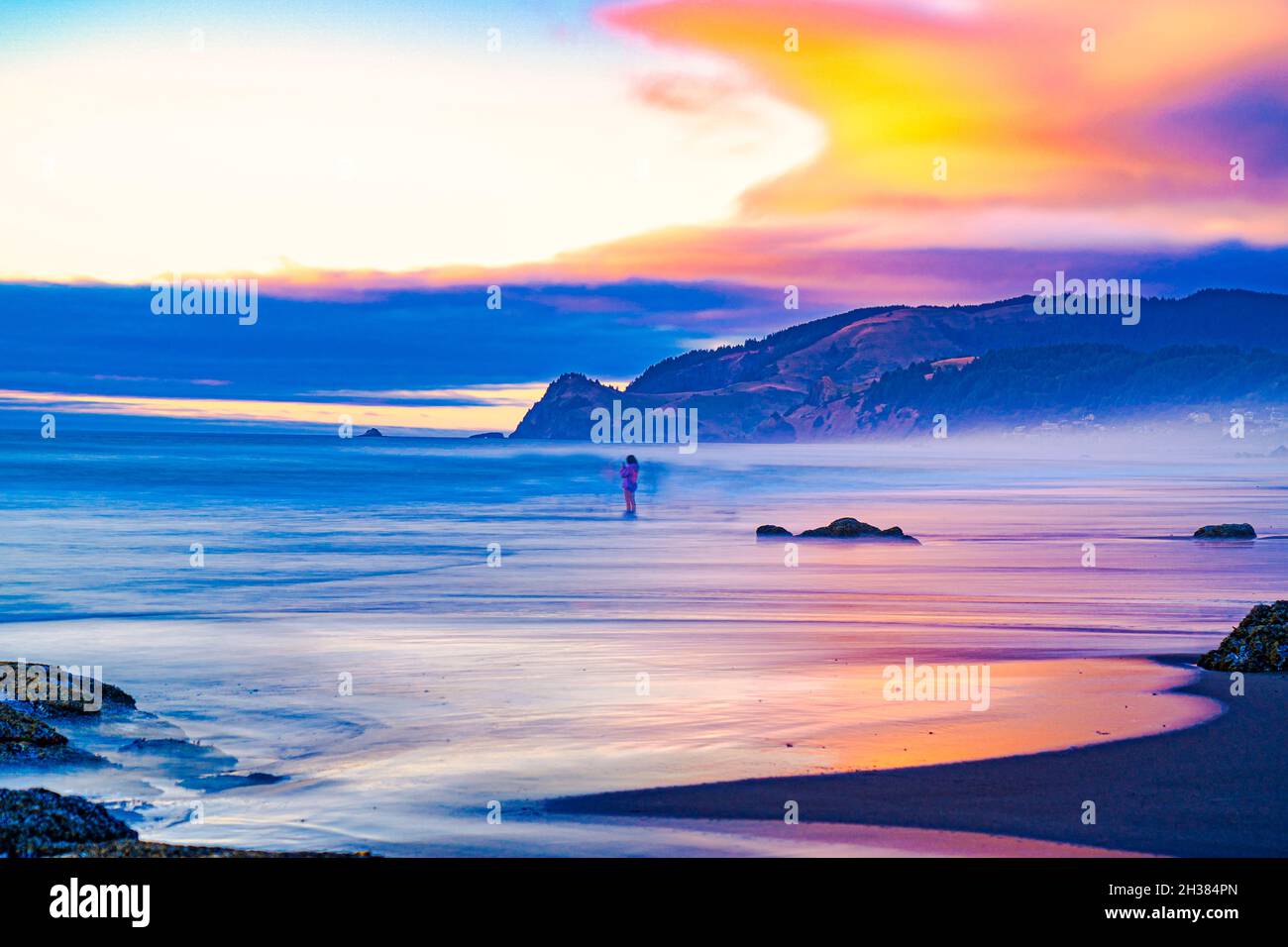 The setting sun colors the clouds above the beach on the Oregon coast ...