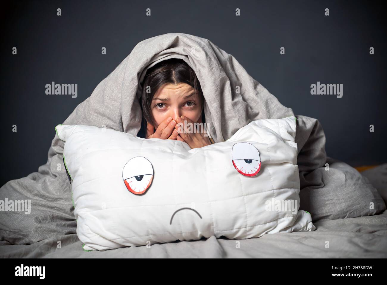 Cute sad young girl hugs a white pillow with painted eyes and face ...