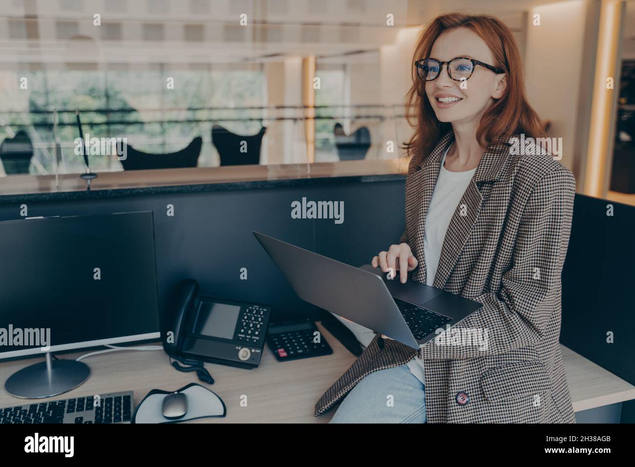 Woman in casual clothes sitting on desk in her cubicle in office while ...