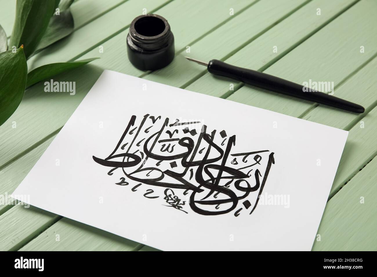 Paper with Arabic text and tools for calligraphy on wooden background ...